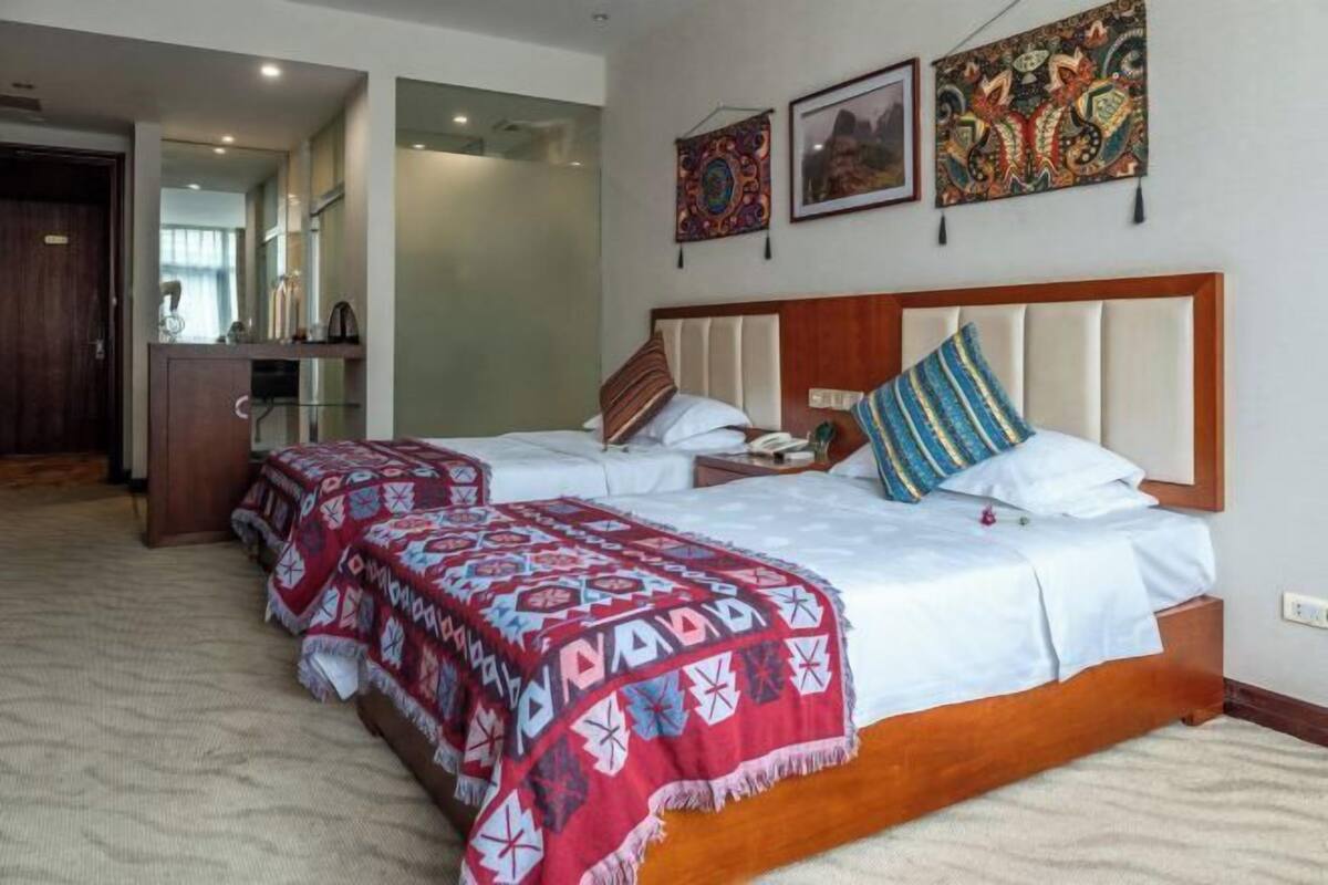 Quarto de hotel com duas camas, uma cabeceira de madeira, uma escrivaninha e um espelho.