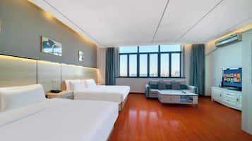 Quarto de hotel com duas camas, um sofá, uma TV e vista para a cidade.