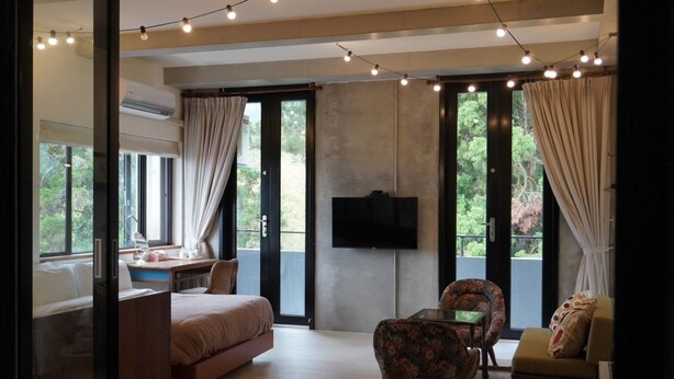 Quarto moderno com cama, escrivaninha e televisão. Há cortinas, uma janela e uma varanda com vista.