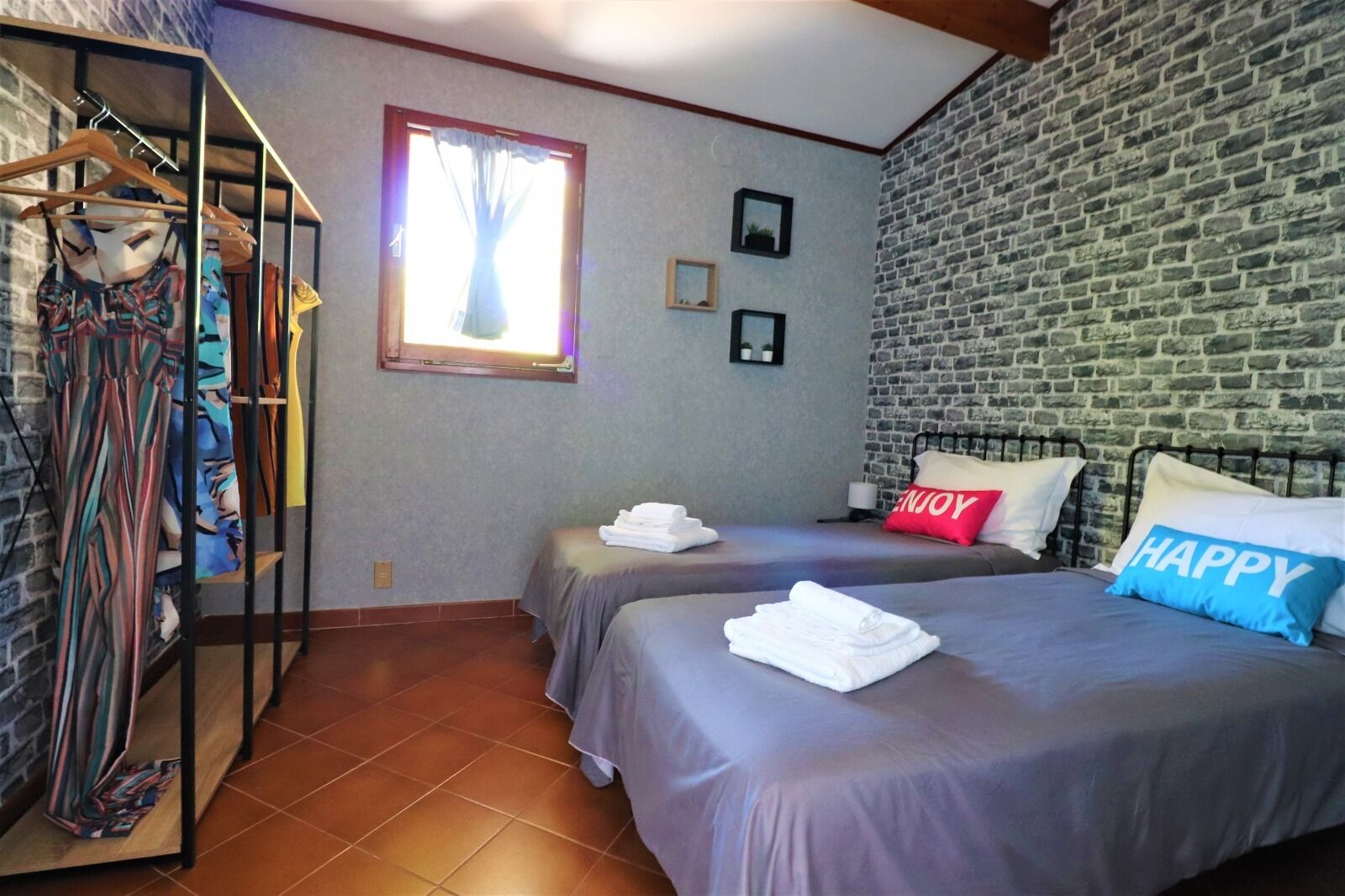 Quarto com duas camas, um guarda-roupa, uma janela e uma parede de tijolos.