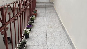 Um corredor estreito com corrimão de metal vermelho, plantas em vasos e uma porta branca no final.