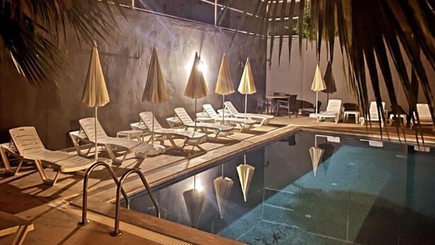 Piscina interna com espreguiçadeiras e guarda-sóis, cercada por palmeiras.