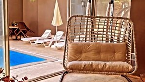 Uma cadeira de vime com assento acolchoado em um quarto iluminado pelo sol e vista para uma piscina.