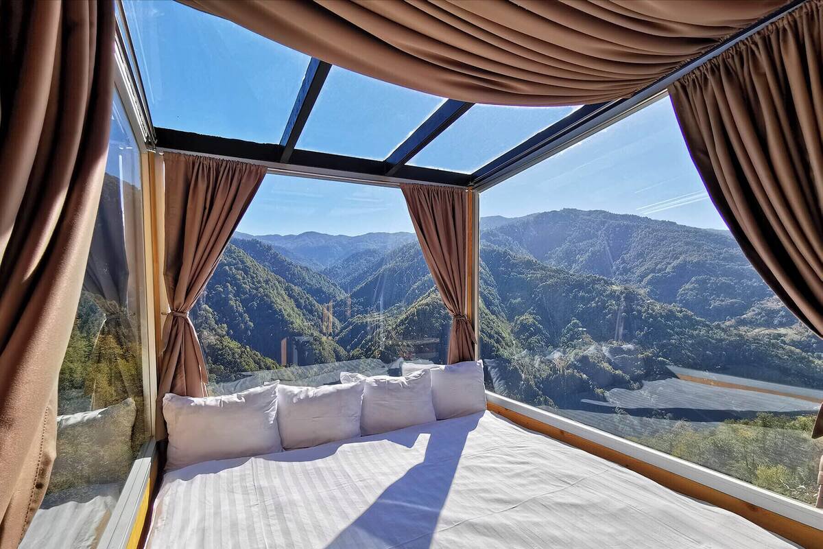 Quarto com uma grande janela com vista para uma paisagem montanhosa.