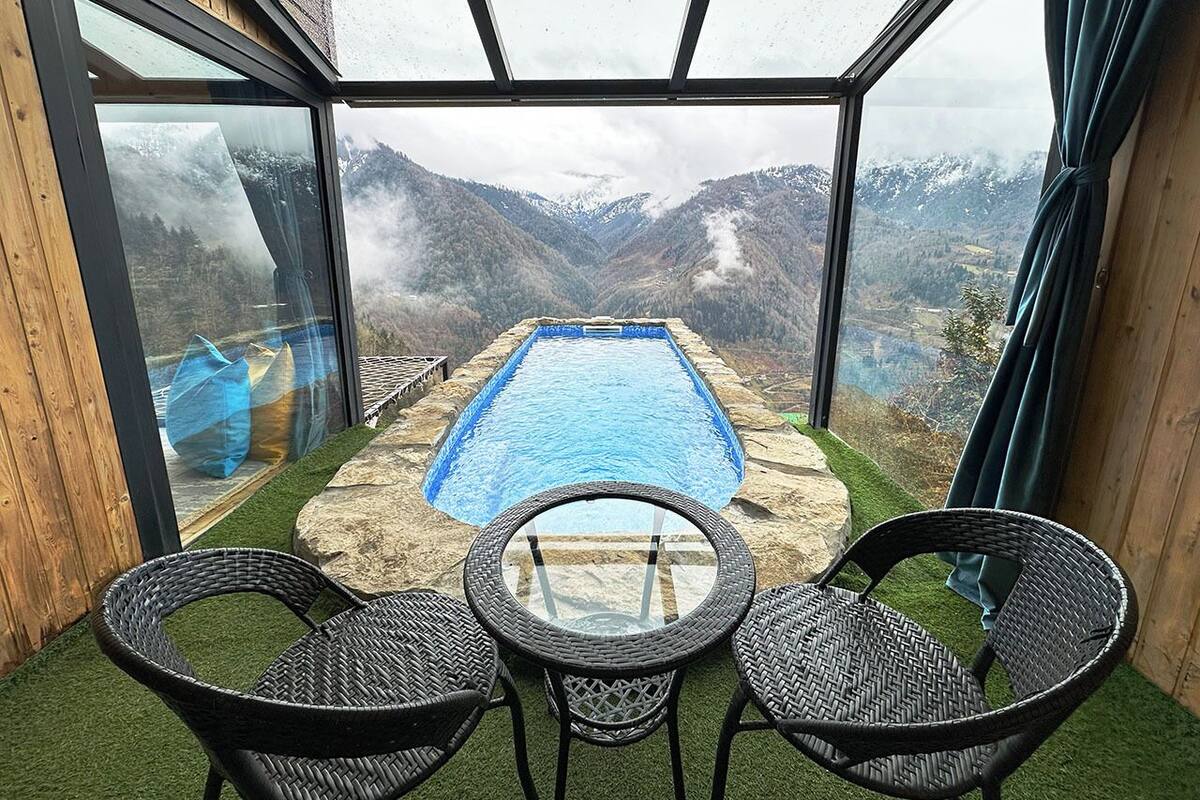 Piscina com vista para montanhas, rodeada por cadeiras de vime e uma mesa de vidro.