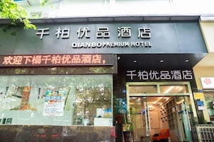 Entrada de hotel com uma placa indicando 'Qianbo Premium Hotel' e uma porta de vidro.