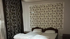 Quarto com cama de madeira, duas mesas de cabeceira, tapeçaria estampada na parede e cortina com padrão em espiral.