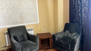 Duas poltronas cinza escuro com almofadas, uma pequena mesa de madeira lateral e um radiador na parede.