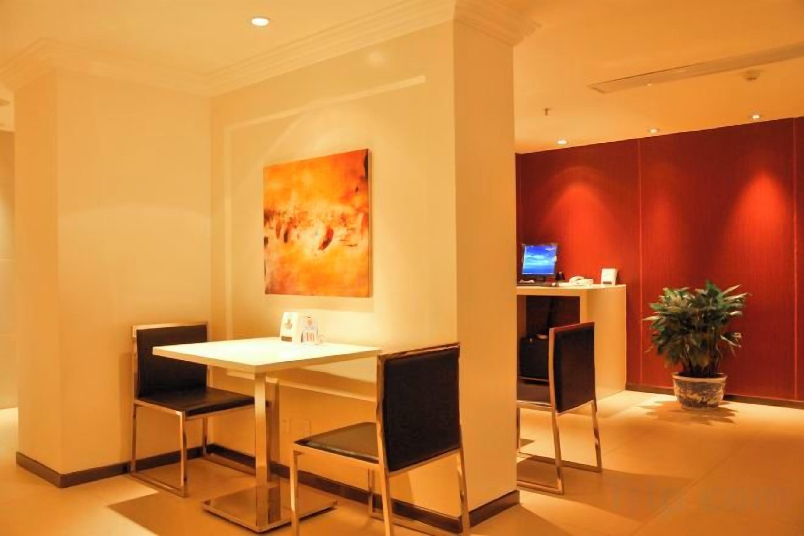 Um hall de hotel com balcão de recepção, área de estar com mesa e cadeiras, e um vaso de planta.