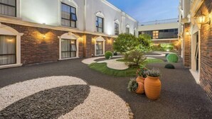 Um pátio com muro de tijolos, uma árvore e um jardim em formato circular.