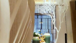 Um corredor com design moderno, apresentando uma escultura de árvore branca e uma série de objetos cilíndricos verdes e brancos, possivelmente elementos decorativos ou mobiliário.
