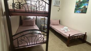 Quarto com uma cama beliche e uma cama de solteiro, ambos com roupa de cama rosa. Há um aparelho de ar condicionado branco na parede e um quadro sobre a cama de solteiro.