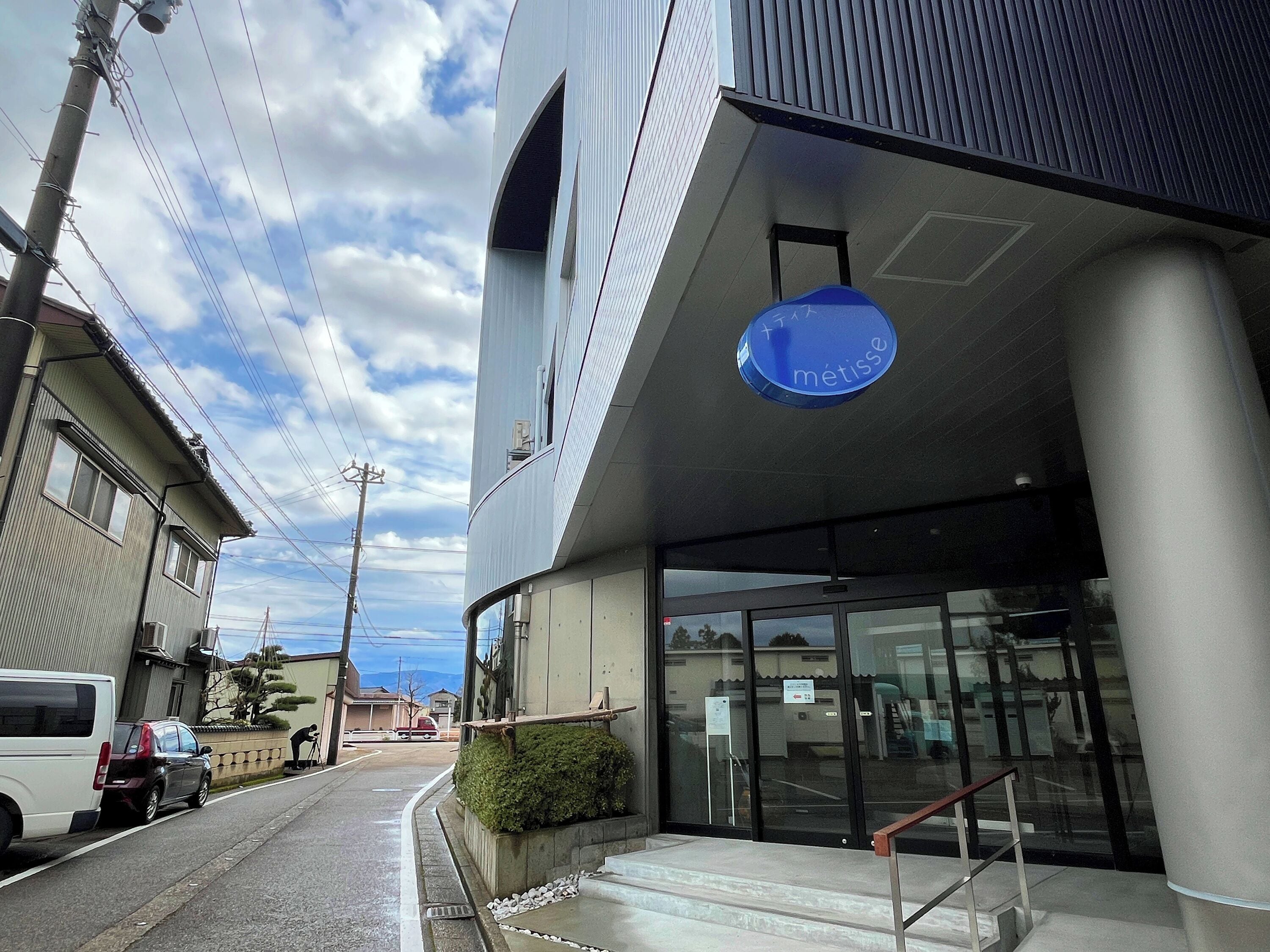 Um edifício moderno com uma grande entrada de vidro, um letreiro azul com o texto "métisse" e um céu claro.