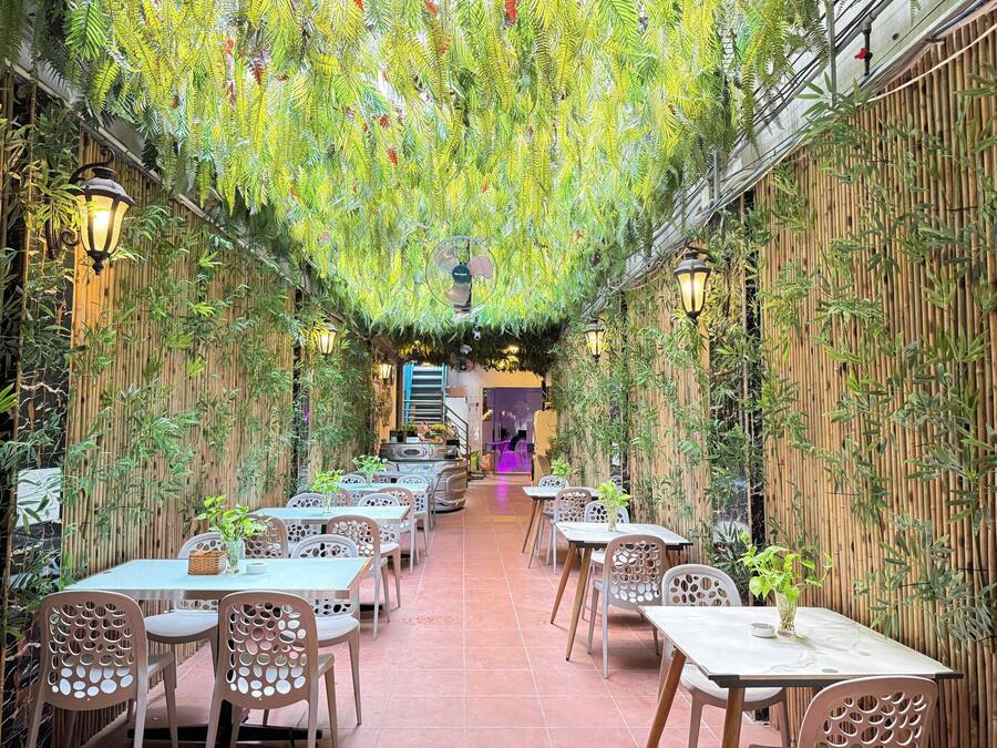 Restaurante com paredes de bambu e plantas penduradas, com mesas e cadeiras de design moderno.