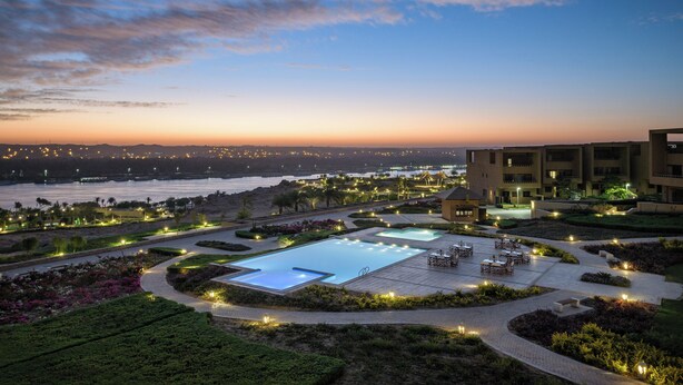 Um resort com uma piscina grande, área de estar externa e vista para o oceano ao entardecer.