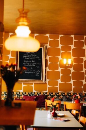 Interior de restaurante com menu em lousa, parede estampada e móveis de madeira.