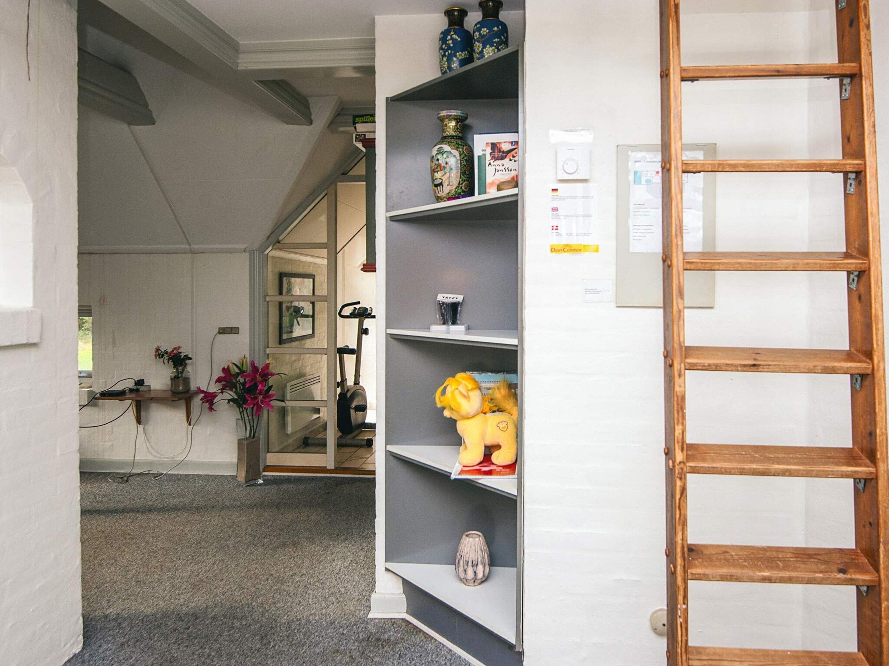 Um quarto com uma escada de madeira, uma estante com objetos decorativos e uma porta que dá para outro cômodo.