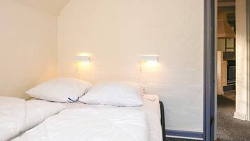 Quarto com cama, duas luminárias na parede e porta para outro cômodo.