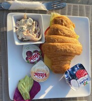 Um prato com croissants, uma salada numa tigela e dois potes de iogurte.