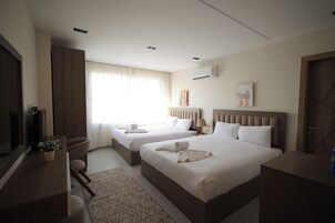 Quarto de hotel com duas camas, televisão, escrivaninha e janela com cortinas.