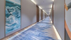 Um corredor comprido e estreito, com carpete estampado e obras de arte nas paredes.