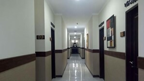 Um corredor de hotel com portas numeradas 99 e 100, piso polido e obras de arte emolduradas nas paredes.