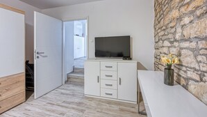 Quarto moderno com parede de pedra, TV de tela plana sobre um móvel, escrivaninha branca e porta de madeira.