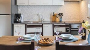 Cozinha moderna com armários brancos, coifa de aço inoxidável e uma mesa de jantar posta com pratos, copos e uma garrafa de vinho.