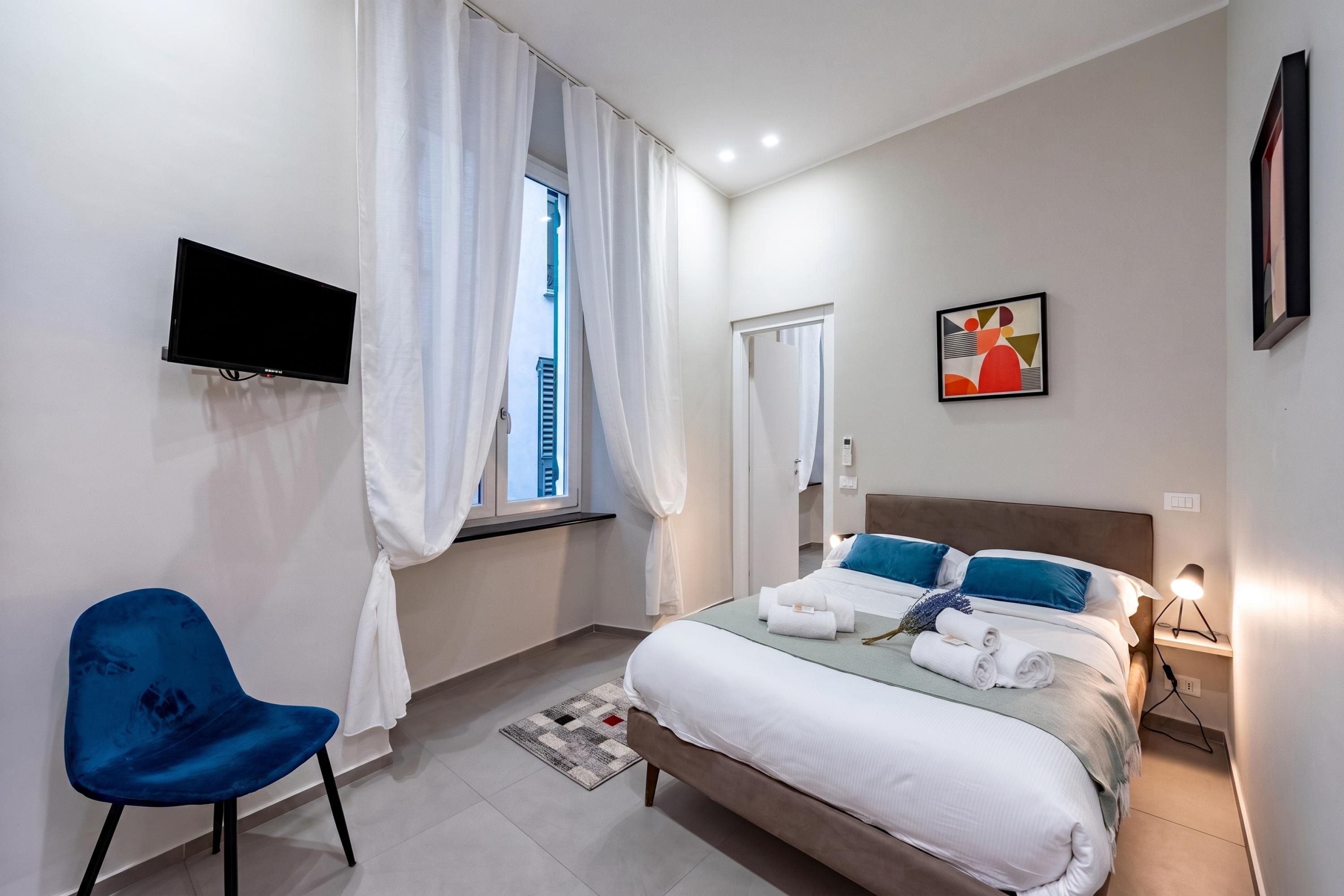 Quarto de hotel com cama, uma cadeira, televisão e um quadro na parede.