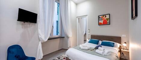 Quarto de hotel com cama, uma cadeira, televisão e um quadro na parede.