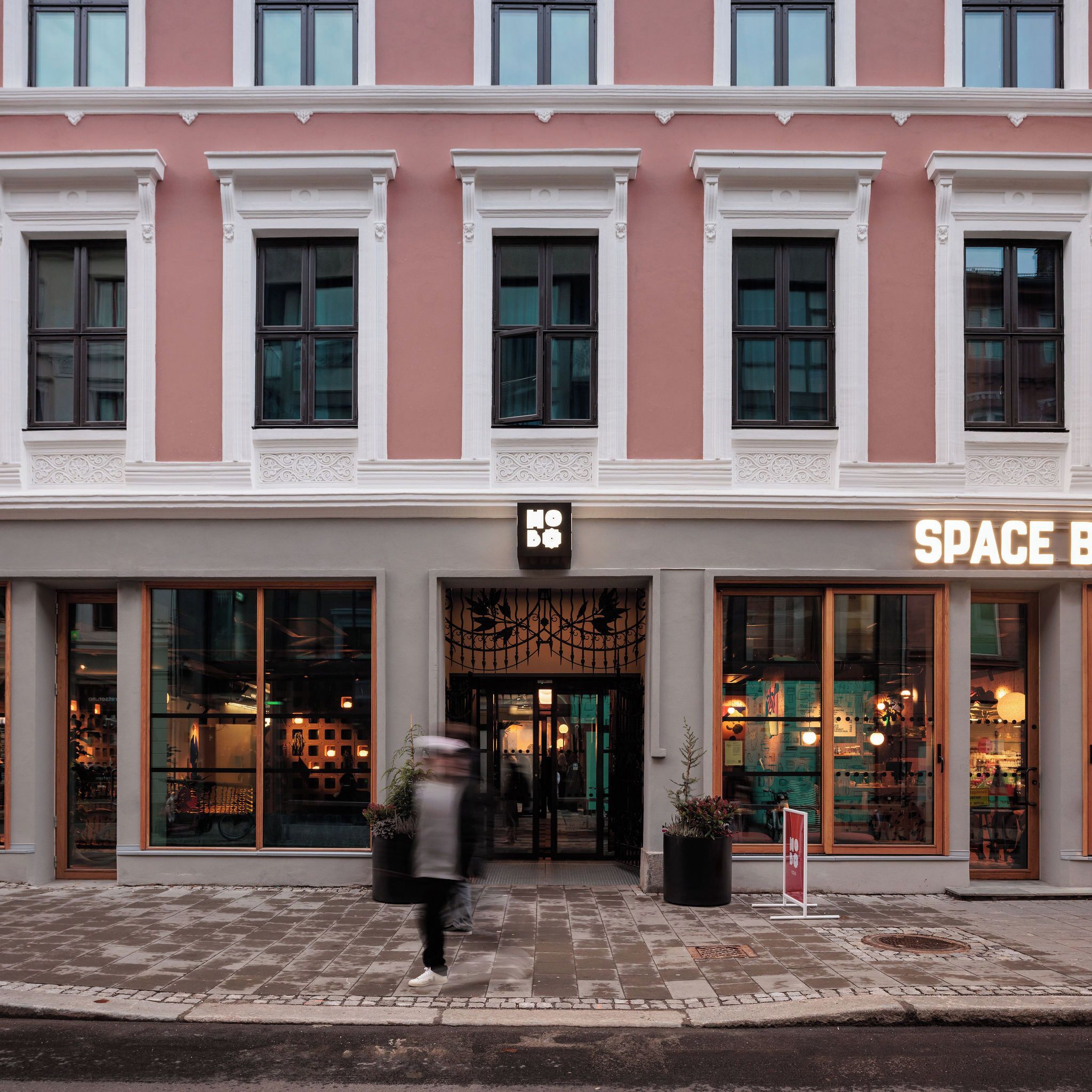 Um edifício com fachada rosa, grandes janelas e uma placa com a inscrição 'SPACE B'.