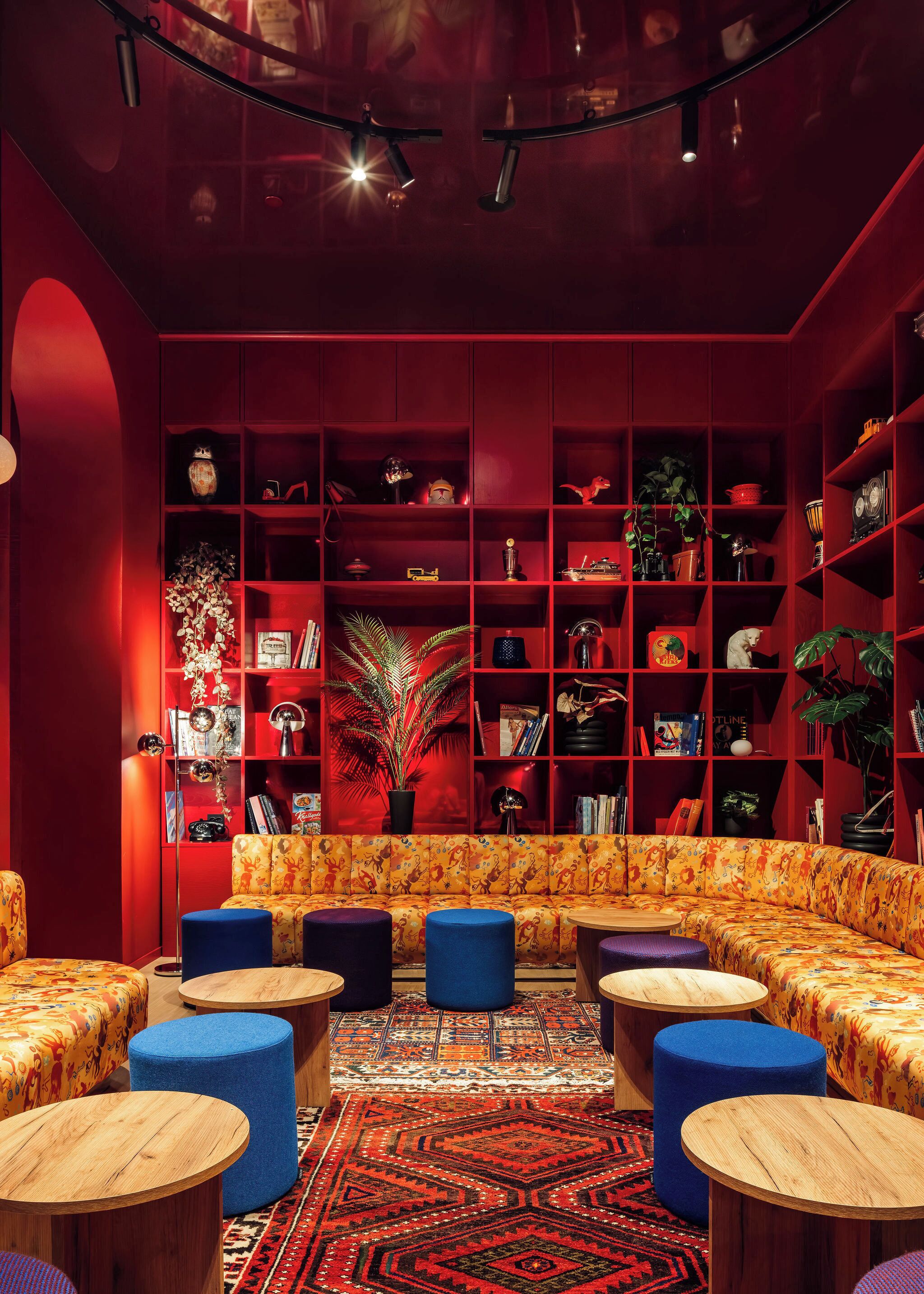 Uma área de estar acolhedora, com decoração em tons de vermelho, um sofá estampado, pufes azuis e um chão coberto por tapete vermelho.
