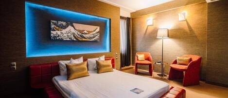 Quarto de hotel moderno com uma cama grande, assentos vermelhos, uma obra de arte na parede e um abajur.