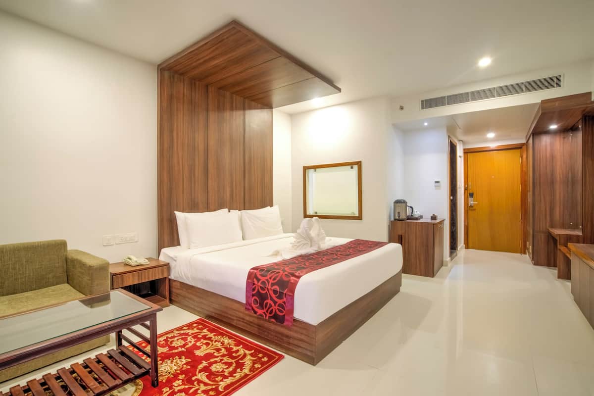 Quarto de hotel com cama, sofá, mesa de cabeceira, cafeteira e guarda-roupa de madeira.