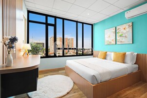 Um quarto moderno com uma janela grande, uma cama com roupa de cama branca, uma mesinha de cabeceira de madeira e um tapete pequeno.