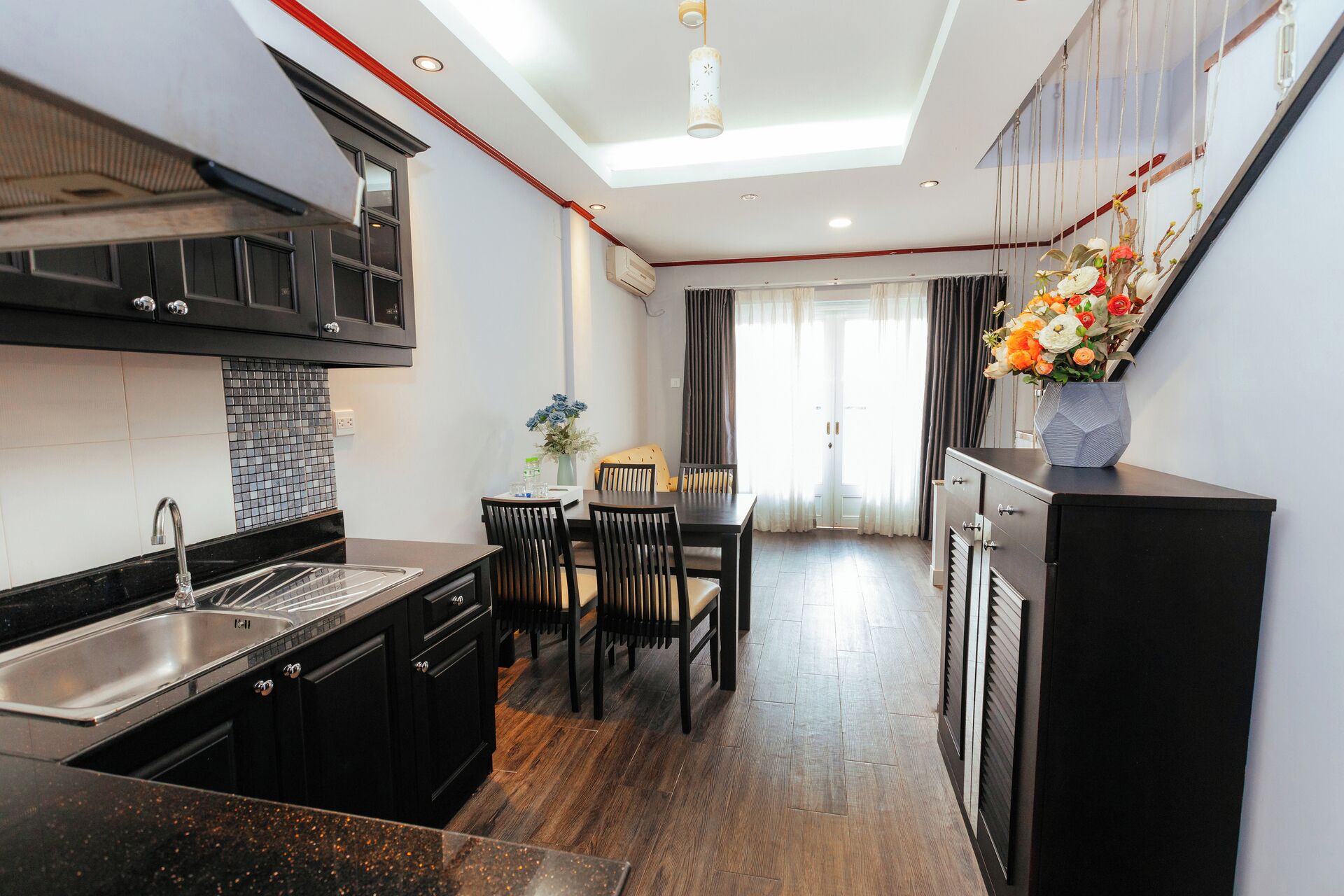 Uma cozinha moderna com armários escuros, uma pia de aço inoxidável e uma área de jantar com mesa e cadeiras.