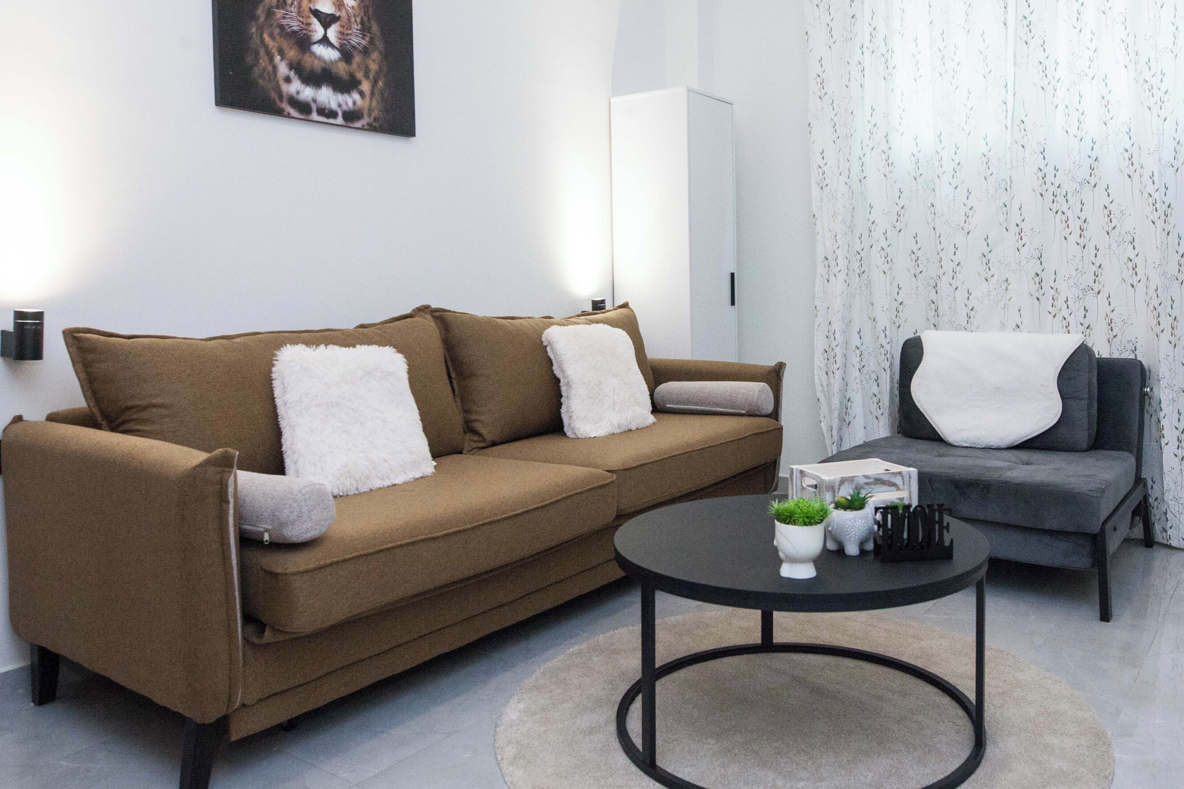 Uma sala de estar moderna com um sofá marrom, uma poltrona cinza, uma mesa de centro redonda com uma planta e uma obra de arte com estampa de leopardo na parede.
