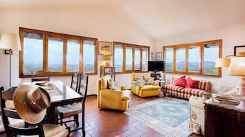 Uma sala de estar espaçosa com uma mesa de jantar de madeira, sofás amarelos e uma grande janela com vista para o campo.
