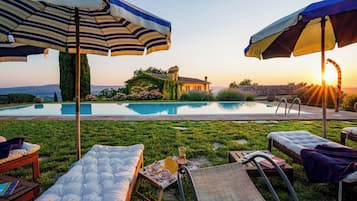 Uma área à beira da piscina com espreguiçadeiras, guarda-sóis e uma mesa com bebidas e petiscos.