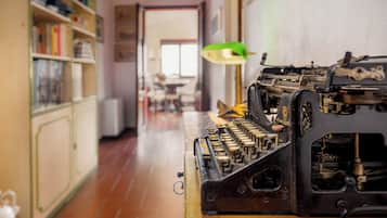 Uma máquina de escrever antiga sobre uma mesa de madeira, num quarto com soalho em azulejos e uma estante cheia de livros.
