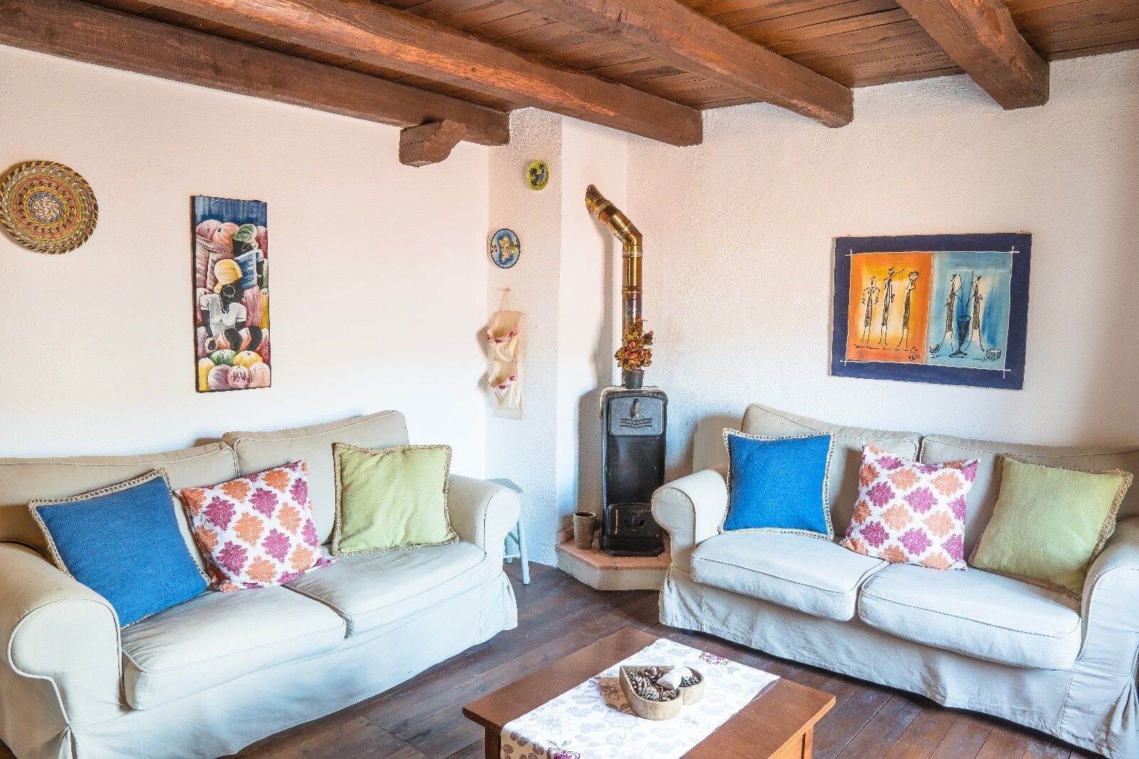 Uma sala de estar aconchegante com dois sofás brancos, almofadas coloridas, uma mesa de centro de madeira e uma lareira decorativa.