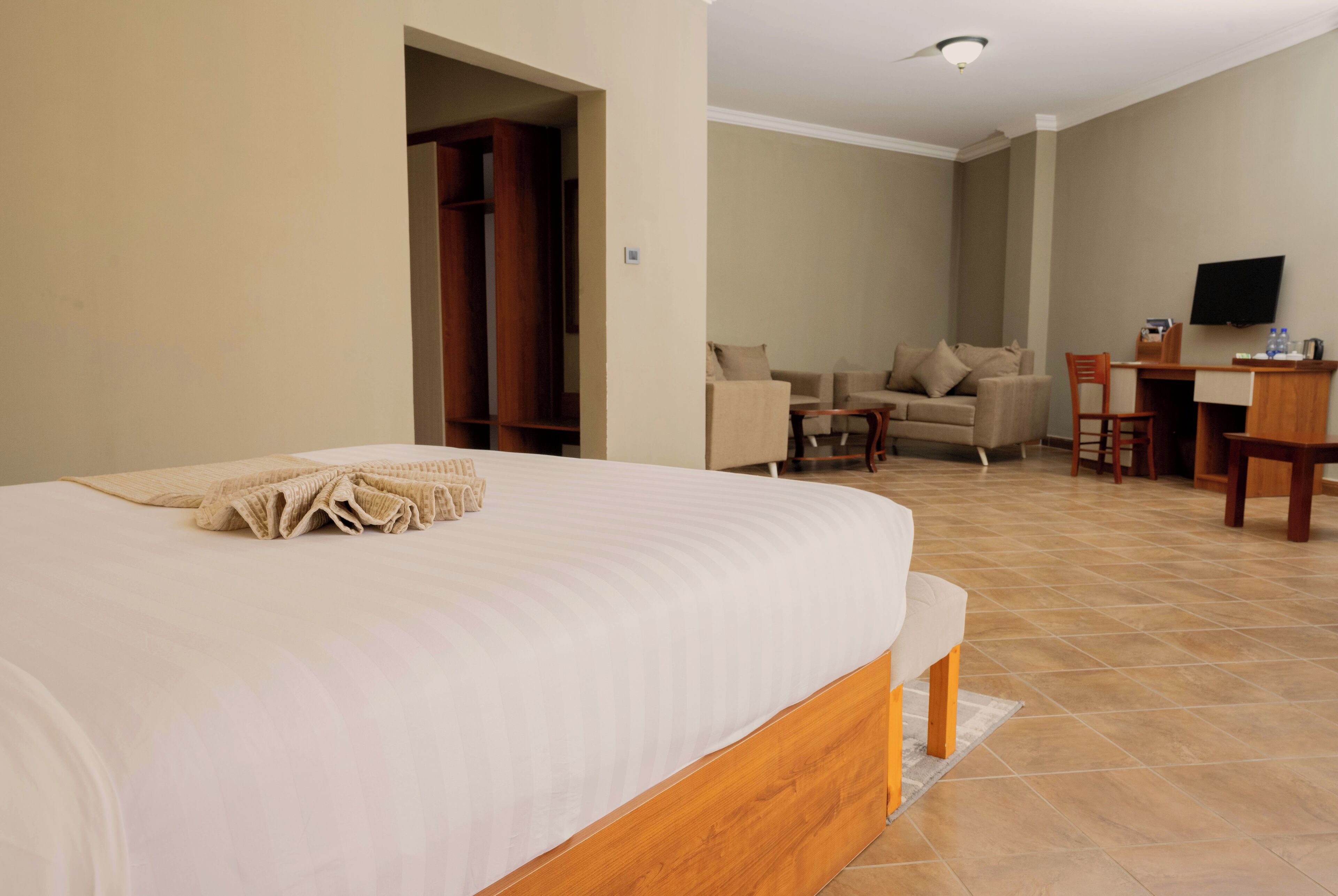 Quarto de hotel com uma cama grande, uma escrivaninha com cadeira, um sofá e uma televisão.