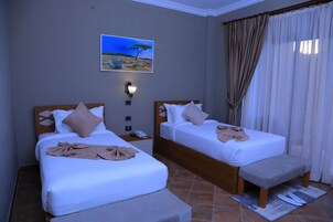 Quarto de hotel com duas camas, mesa de cabeceira com telefone, pintura de paisagem e janela com cortinas.