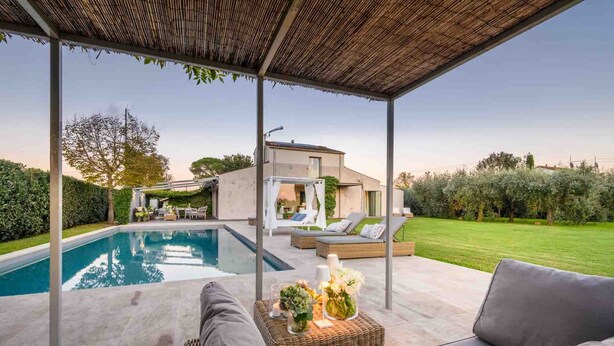 Uma área externa coberta com piscina, assentos e uma casa ao fundo.
