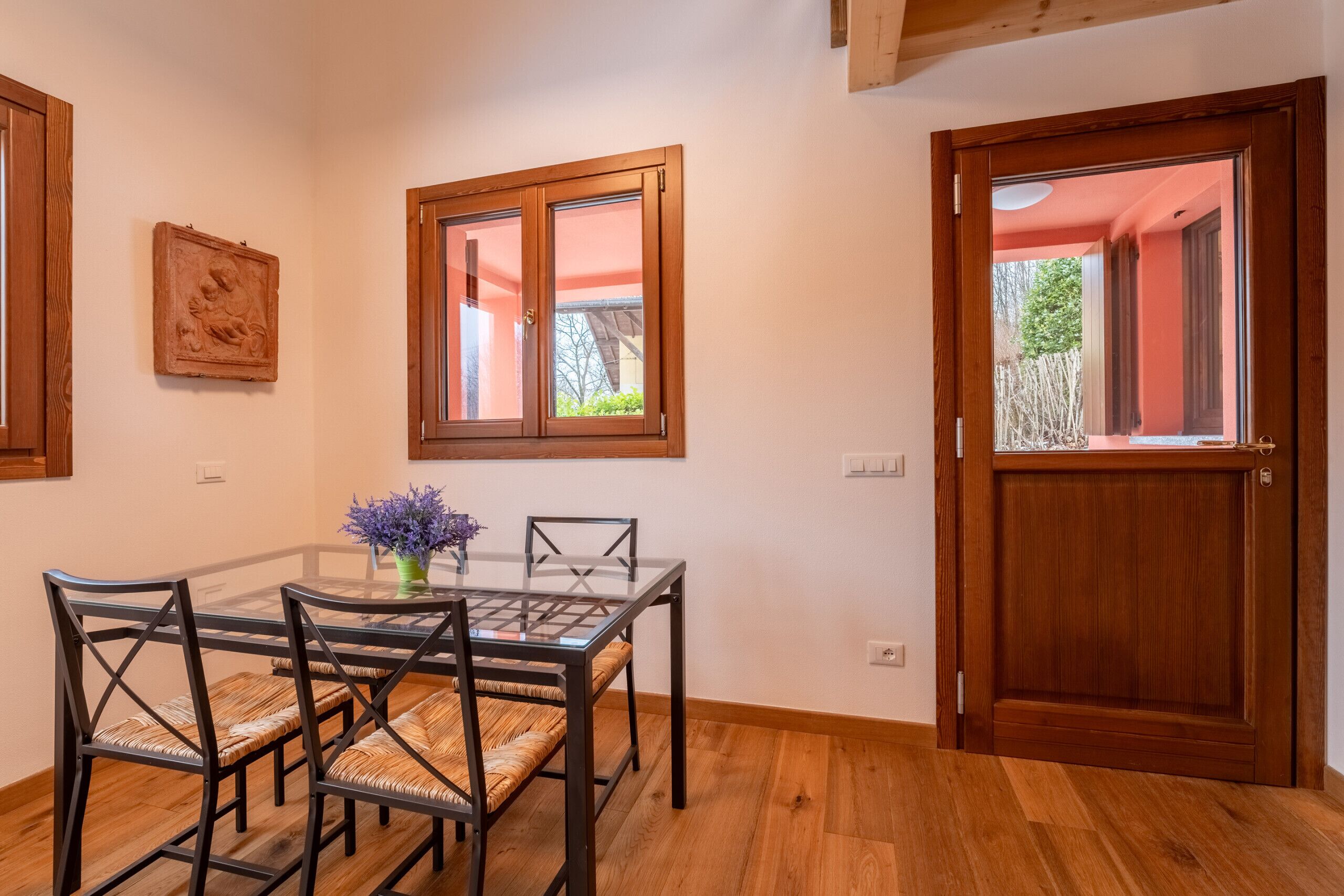 Uma área de refeições com mesa e cadeiras de vidro, porta de madeira e uma obra de arte emoldurada na parede.