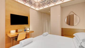 Quarto de hotel com uma cama grande, uma escrivaninha com televisão de tela plana, uma cadeira e uma mesa de cabeceira com abajur.