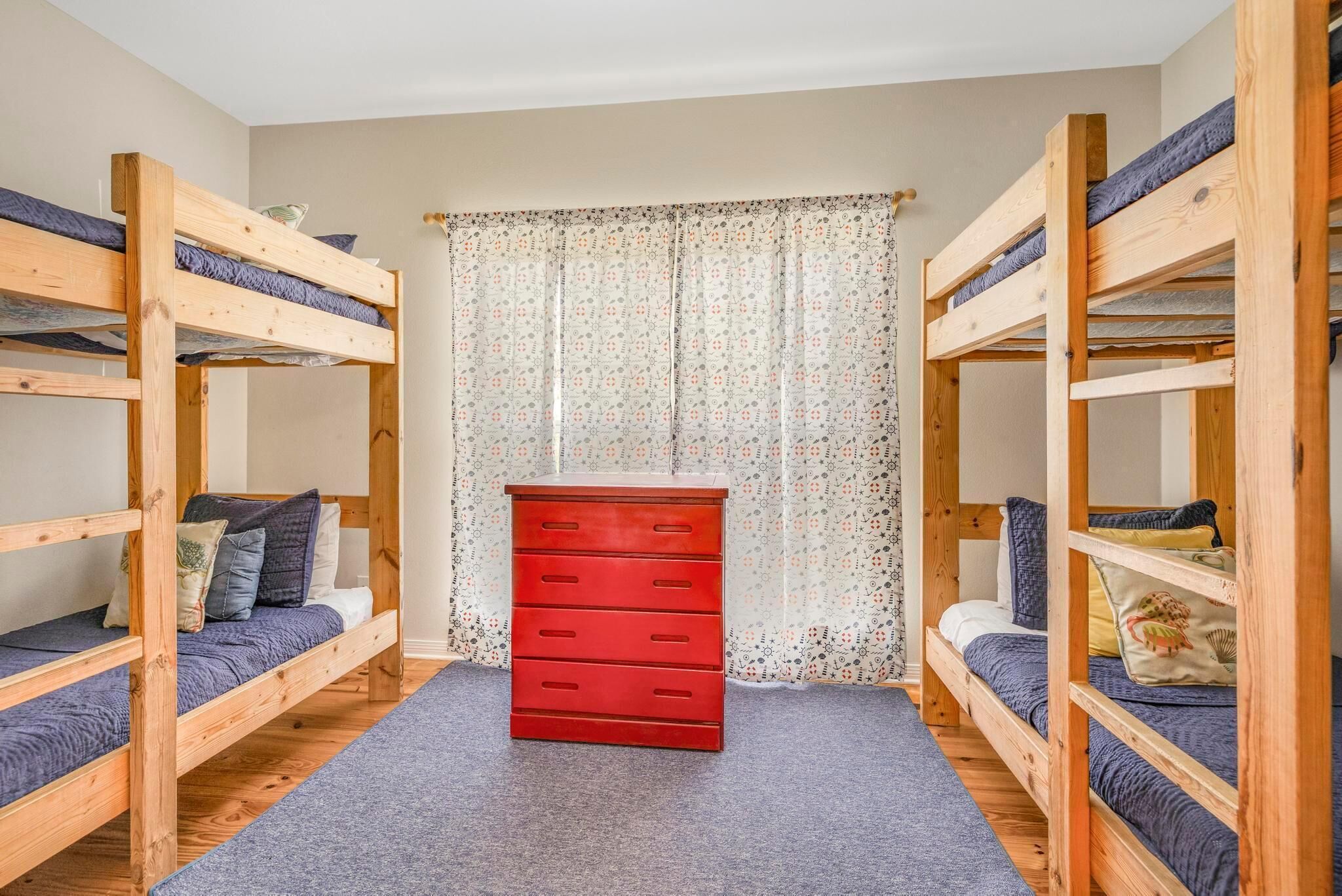 Quarto com beliches, cómoda vermelha e cortina florida.