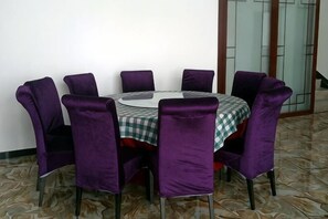 Uma mesa de jantar redonda com oito cadeiras roxas, toalha xadrez e chão ladrilhado.