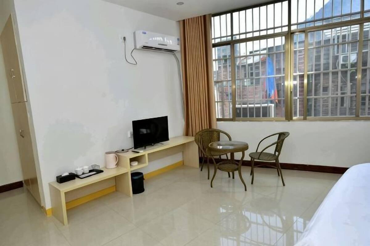 Quarto de hotel com uma cama, uma televisão sobre um suporte, uma janela com cortinas e uma cadeira.