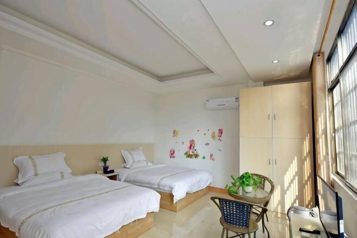 Quarto de hotel com duas camas, uma mesa pequena com uma cadeira, uma janela com cortinas e um guarda-roupa.